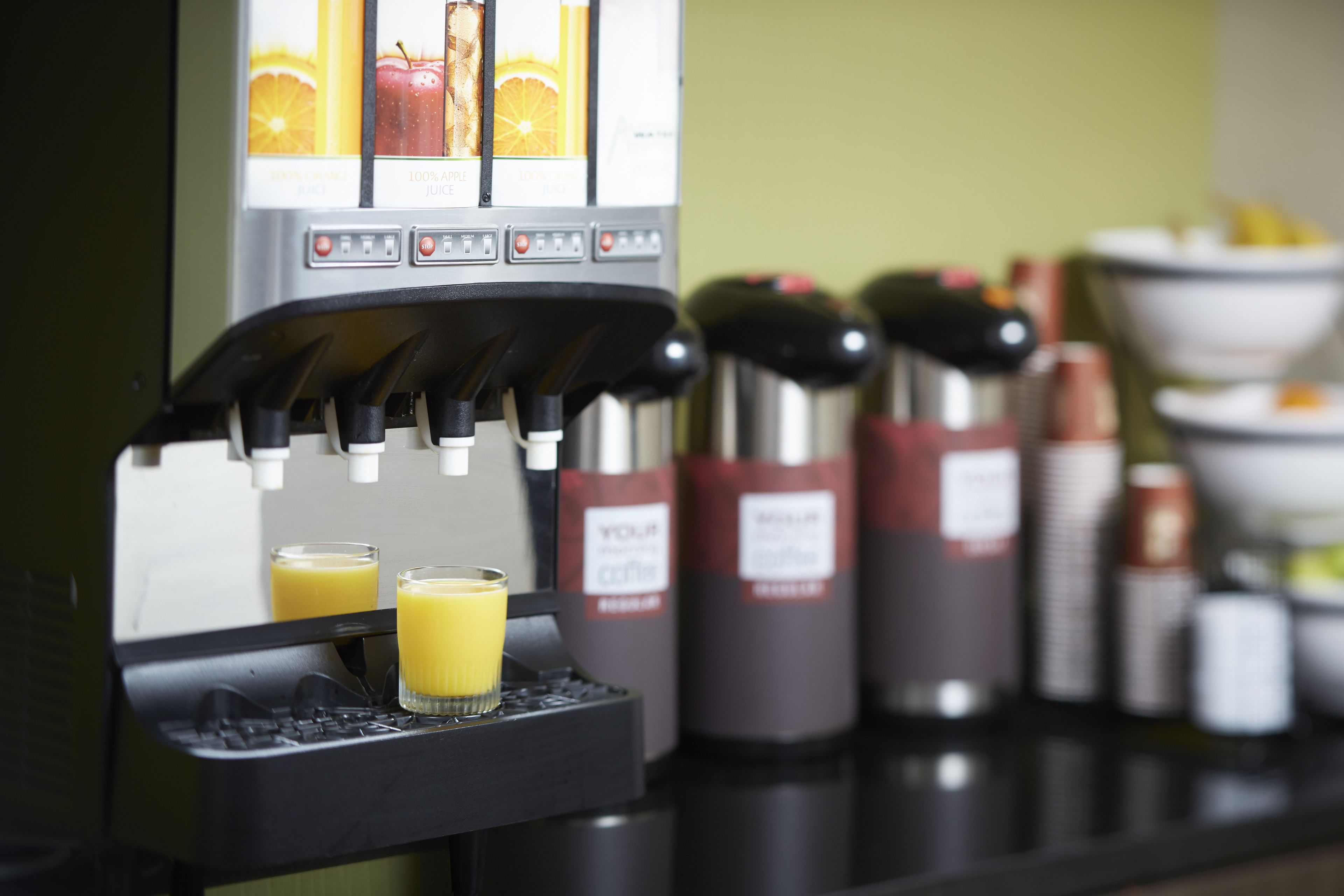 Máquina de café servindo suco de laranja, com diversas opções de café ao fundo.
