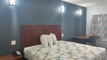Quarto de hotel com uma cama grande, cabeceira de madeira, escrivaninha com cadeira e cortina estampada.