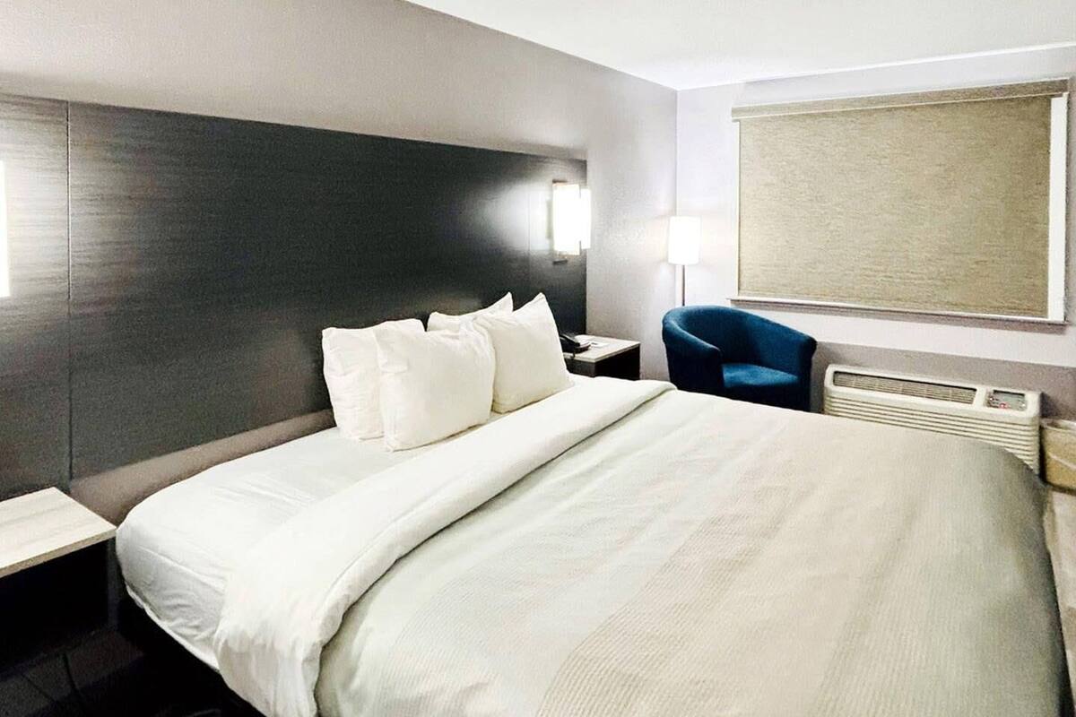 Quarto de hotel com uma cama grande, mesa de cabeceira, cadeira, luminária e radiador.
