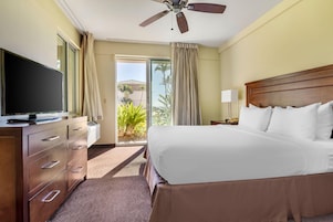 Quarto de hotel com cama, televisão, penteadeira, ventilador de teto e vista para o exterior.