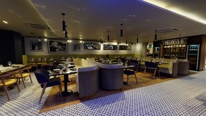 Interior moderno de restaurante com mesas altas, assentos acolchoados e área de bar.