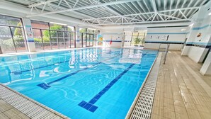 Uma piscina interior com água azul cristalina, paredes revestidas de azulejos e estrutura coberta.