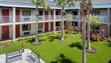 Um motel com um pátio que inclui palmeiras, um banco e um pequeno jardim.
