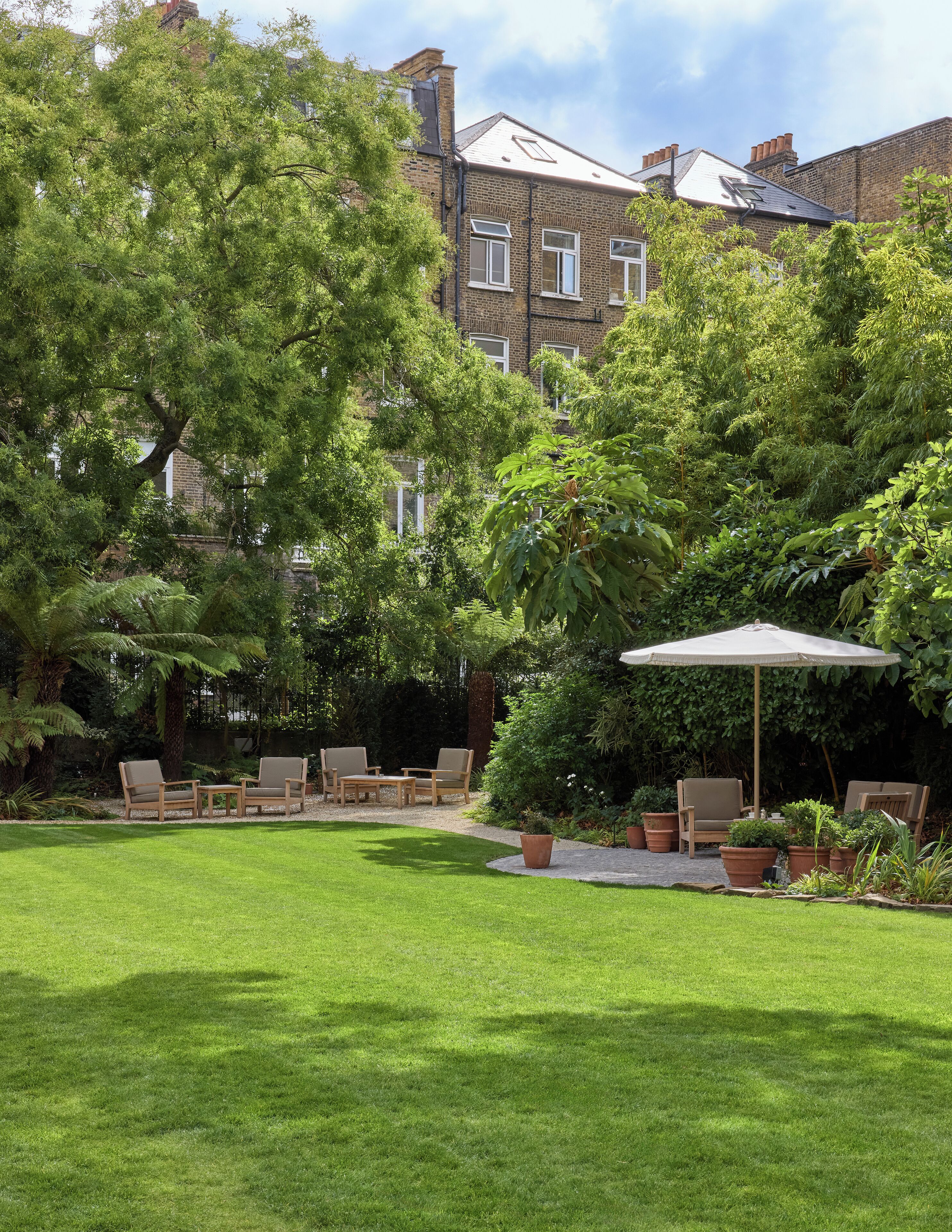Um jardim bem cuidado com gramado, área de estar externa e um grande guarda-sol.