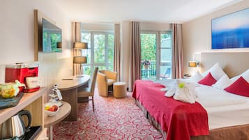 Quarto de hotel com cama, escrivaninha, cadeira, máquina de café, chaleira e vista para o exterior.