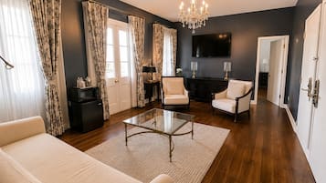 Uma sala de estar com sofá, cadeiras, mesa de centro, TV e lustre.