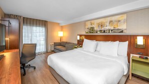 Quarto de hotel com uma cama grande, uma escrivaninha com cadeira, televisão e um quadro na parede.