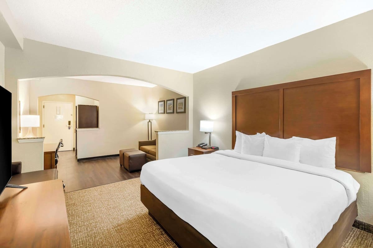 Quarto de hotel com uma cama grande, uma escrivaninha, uma cadeira, uma televisão e um candeeiro.