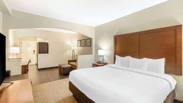 Quarto de hotel com uma cama grande, uma escrivaninha, uma cadeira, uma televisão e um candeeiro.