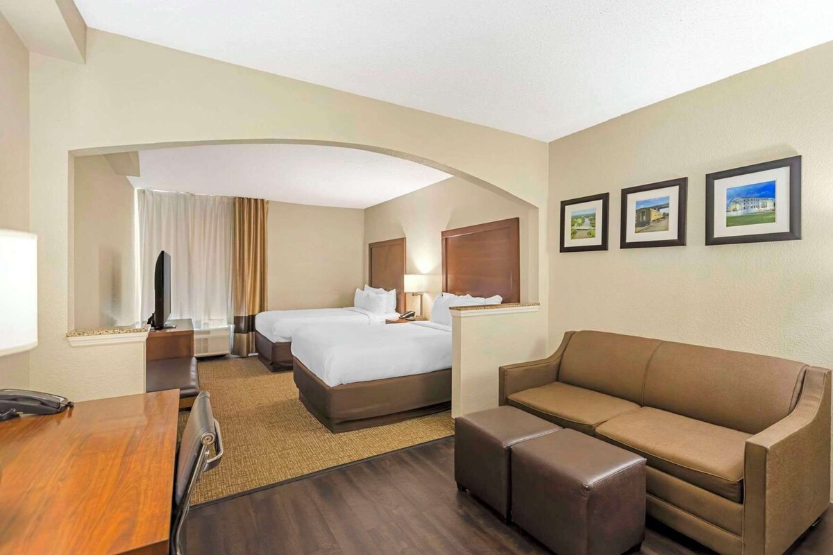 Quarto de hotel com cama, sofá, escrivaninha, televisão e quadros na parede.