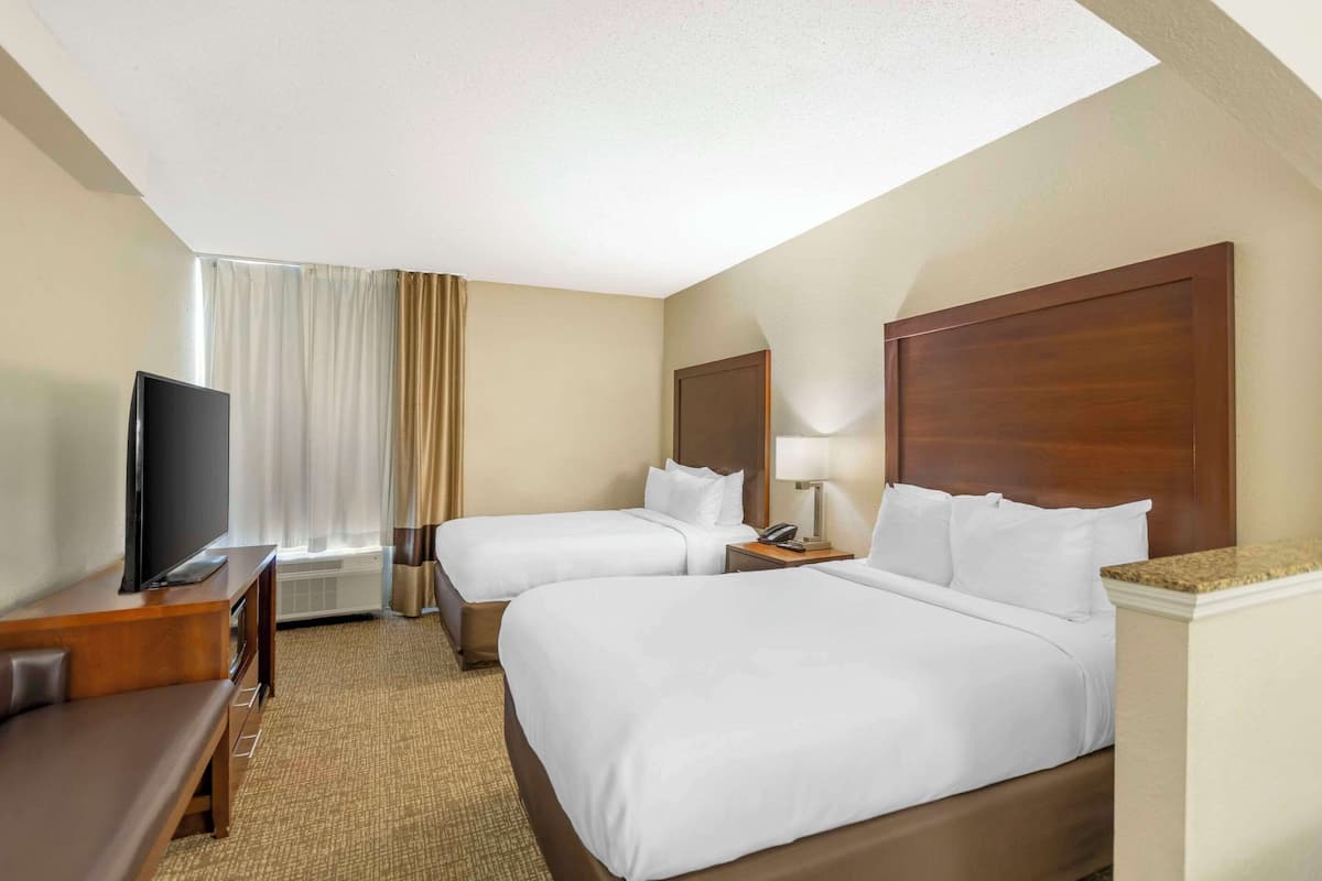 Quarto de hotel com duas camas, televisão, escrivaninha e janela com cortinas.