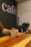 Uma pessoa segurando um copo com uma fatia de fruta em cima de uma mesa de madeira em um café.
