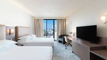 Quarto de hotel com duas camas, uma escrivaninha, televisão e vista para a cidade.