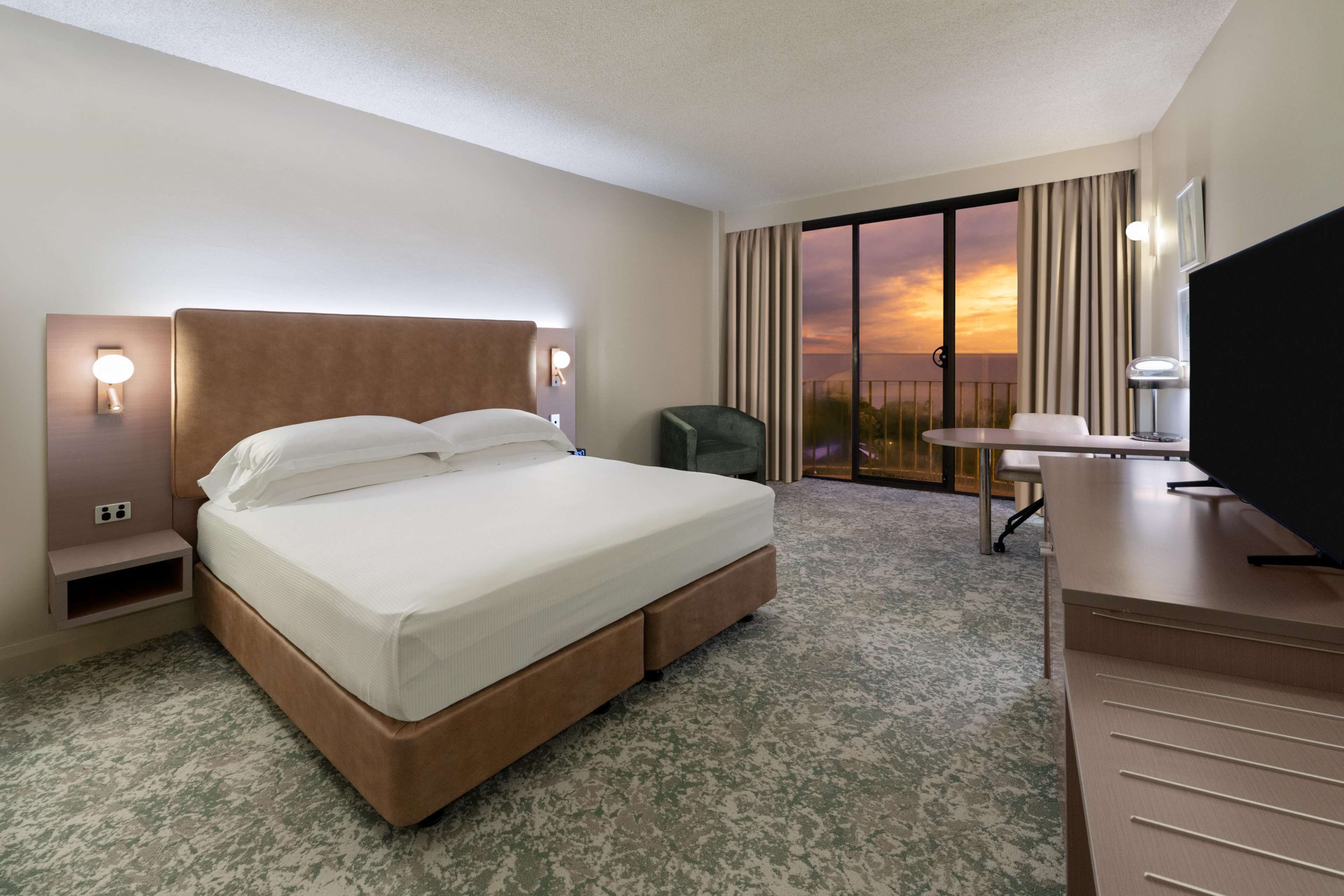Quarto de hotel com uma cama grande, uma escrivaninha, uma cadeira e uma televisão.
