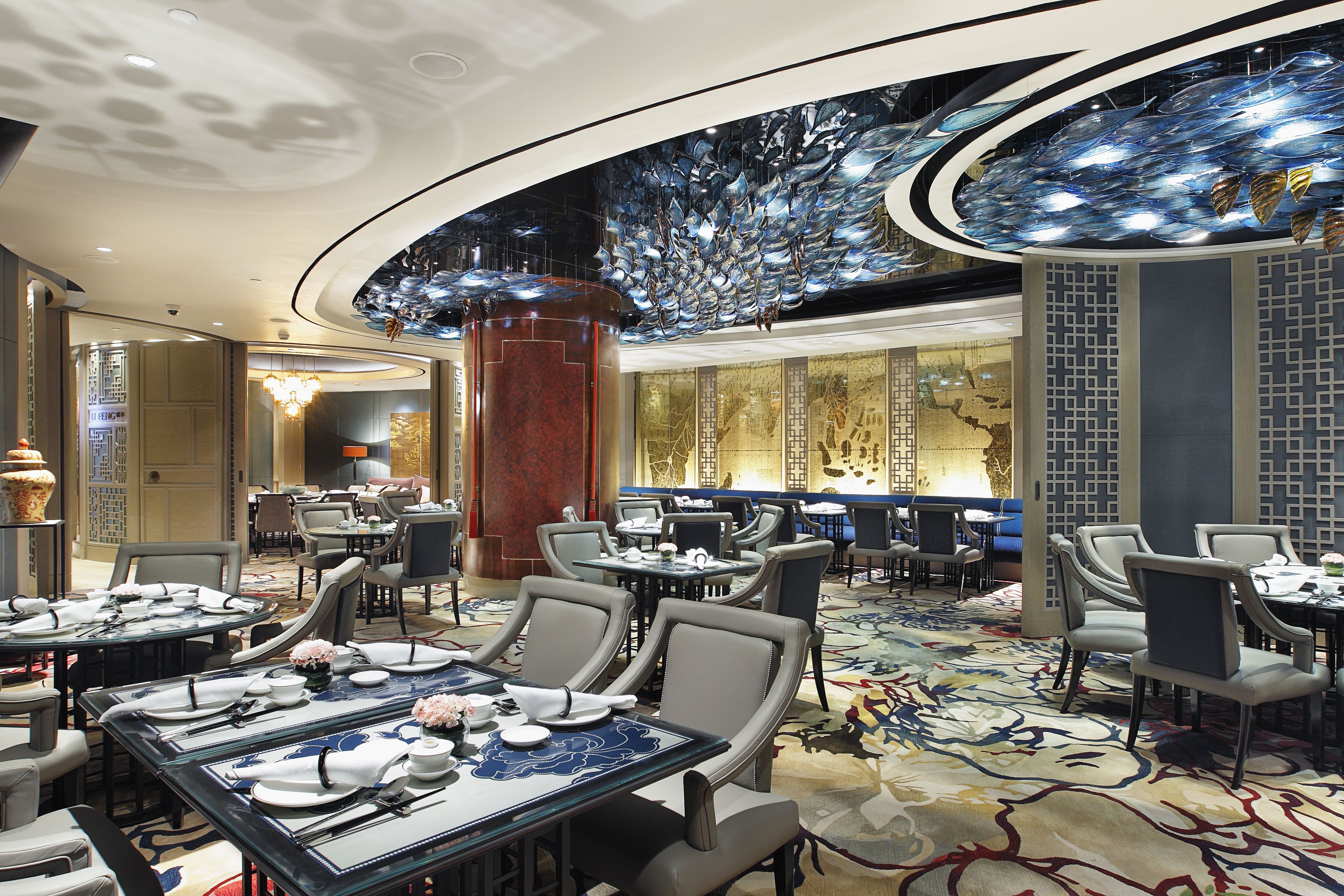 Restaurante moderno com mesas redondas, cadeiras e teto decorativo.