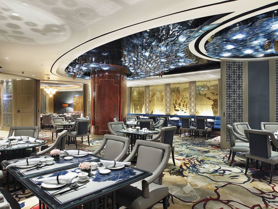 Restaurante moderno com mesas redondas, cadeiras e teto decorativo.