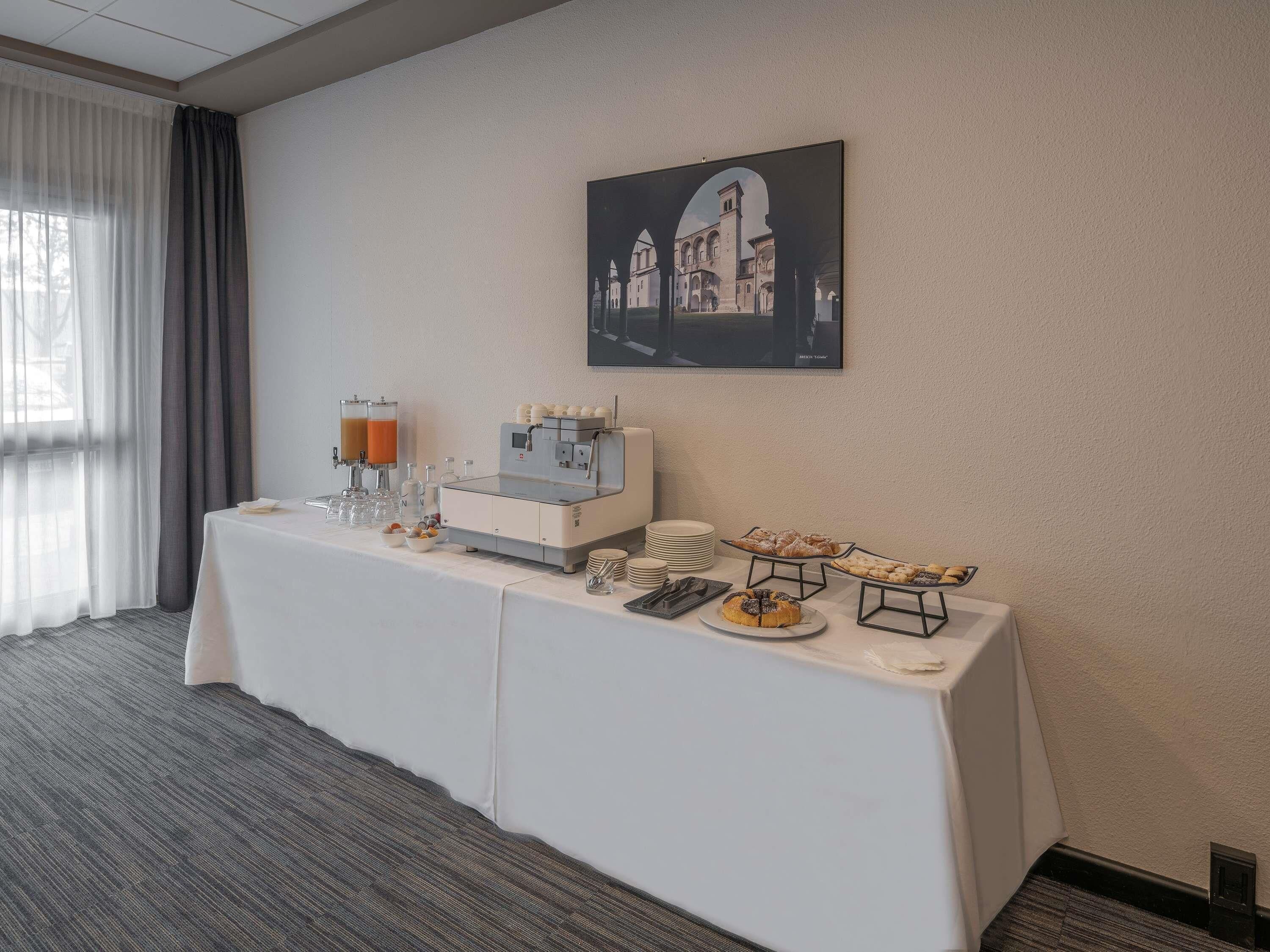 Quarto de hotel com bancada para café da manhã, cafeteira e quadro na parede.