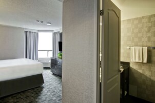Quarto de hotel com cama, penteadeira, banheiro com porta-toalhas e janela com cortinas.