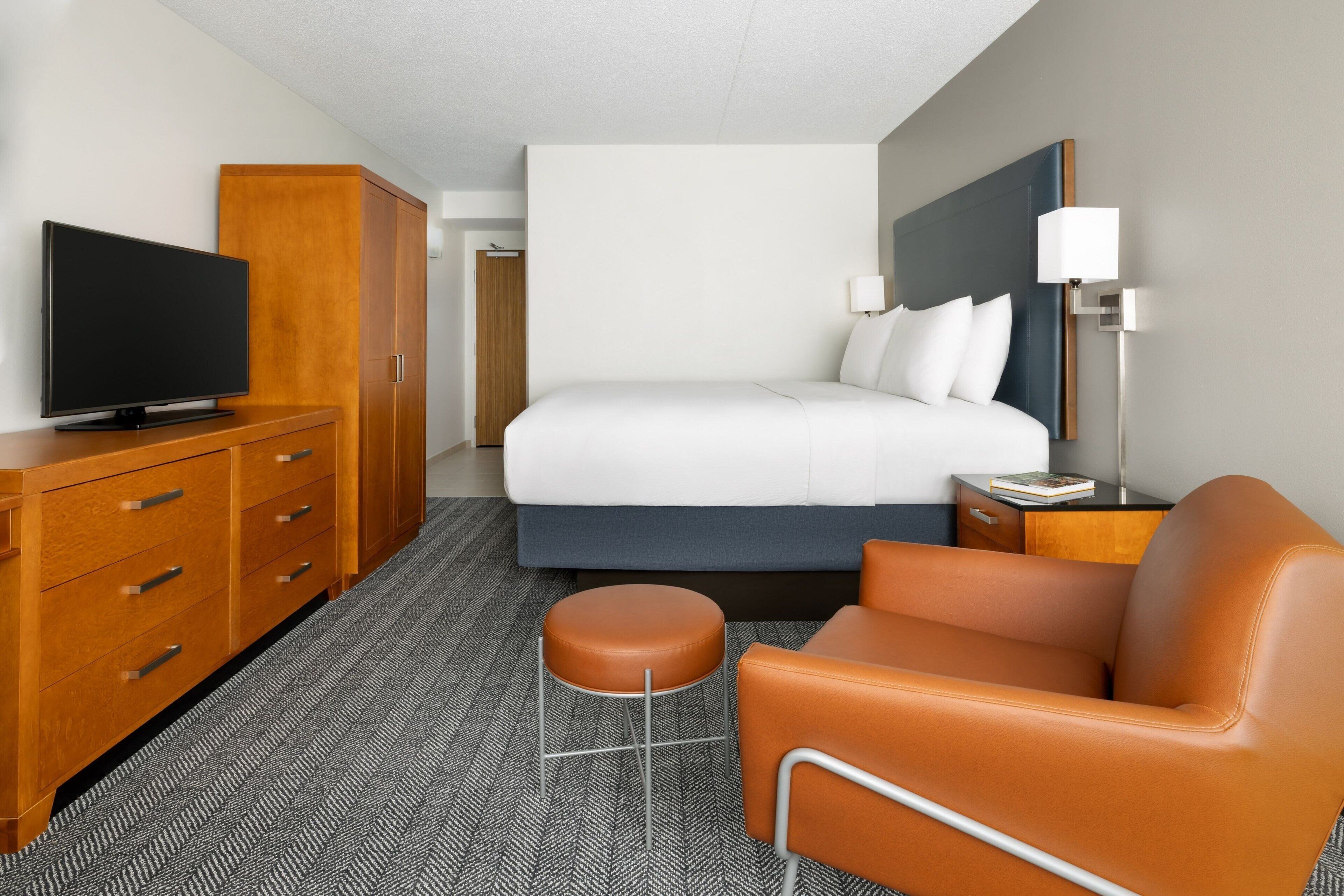 Quarto de hotel com cama, televisão, escrivaninha, cadeira e abajur.
