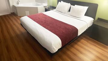 Quarto de hotel com cama, manta vermelha, travesseiro branco, mesa de cabeceira e banheiro com banheira.
