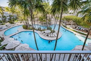 Área de piscina com várias piscinas, espreguiçadeiras e palmeiras.