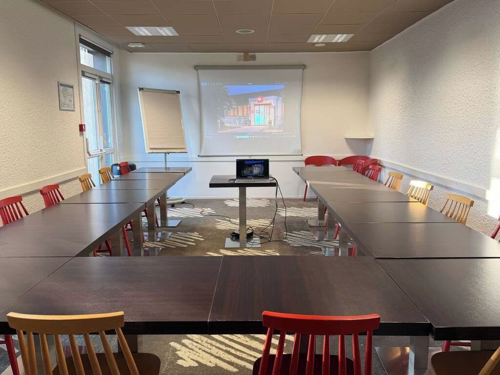 Sala de conferência com uma mesa comprida, cadeiras, tela de projetor e apresentação.