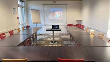 Sala de conferência com uma mesa comprida, cadeiras, tela de projetor e apresentação.