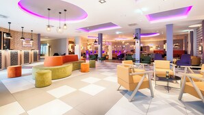 Um lobby moderno de hotel com chão quadriculado, áreas de estar e uma mesa de recepção.