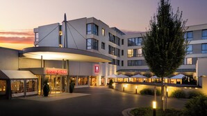 Hotel com design moderno, destacando uma entrada curvada, vários andares e área externa bem iluminada com guarda-sóis.