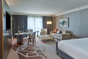 Quarto de hotel com cama, sofá, escrivaninha com cadeira, televisão e um quadro na parede.