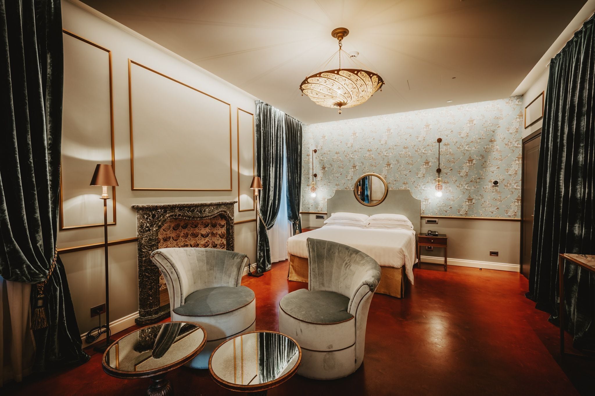 Quarto com uma cama, duas poltronas, uma mesa redonda, um espelho, lareira e um candelabro.