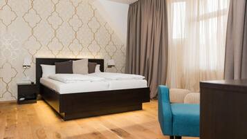 Quarto moderno com cama grande, mesas de cabeceira, uma cadeira azul e papel de parede estampado.