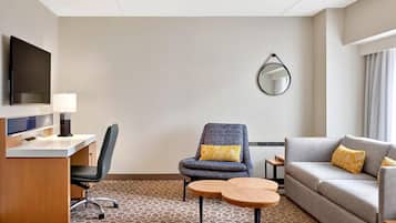 Quarto de hotel com escrivaninha, cadeira, sofá, duas mesinhas, televisão e espelho.