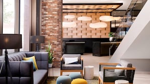 Uma sala de estar moderna com sofá, poltronas e mesa de centro. Apresenta uma parede de tijolos, uma escada e uma grande janela.