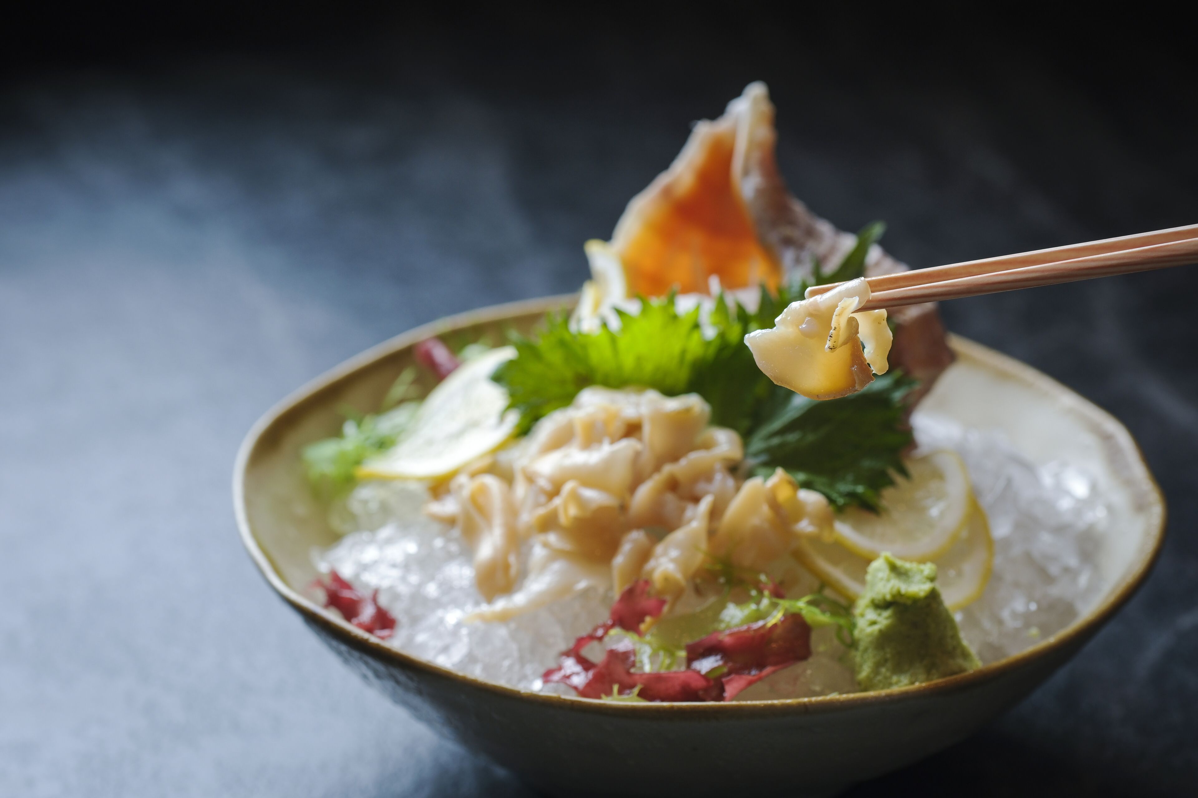 Uma tigela de ramen com vários acompanhamentos e um pedaço de peixe sendo segurado por pauzinhos.