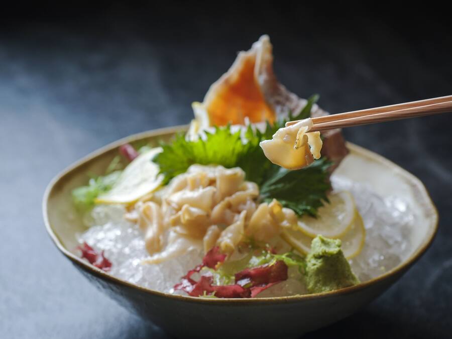 Uma tigela de ramen com vários acompanhamentos e um pedaço de peixe sendo segurado por pauzinhos.