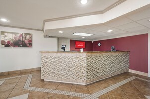 Uma área de recepção com balcão revestido de azulejos, um ecrã digital a exibir 'Wi-Fi Gratuito em Todos os Quartos' e um relógio na parede.