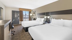 Quarto de hotel com duas camas, uma escrivaninha, uma cadeira, um abajur e uma janela com cortinas.