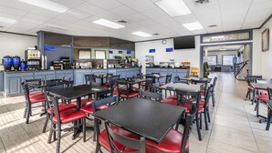 Uma cafeteria ampla com várias mesas e cadeiras, uma área de cozinha e uma escada que dá acesso a outro andar.