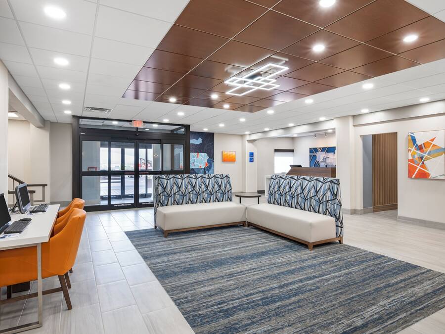 Um lobby moderno com balcão de atendimento, área de estar e uma grande porta de vidro.