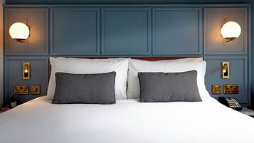 Quarto de hotel com cama grande, duas luminárias fixadas na parede e mesa de cabeceira com telefone.