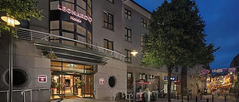 Entrada de hotel com uma placa indicando 'LEONARDO HOTEL' e uma escadaria que leva à porta.