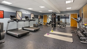 Academia com esteiras, máquinas de musculação e colchonetes.