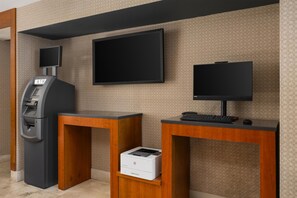 Uma área de recepção com televisão de tela plana, caixa eletrônico, impressora e teclado em mesas de madeira.