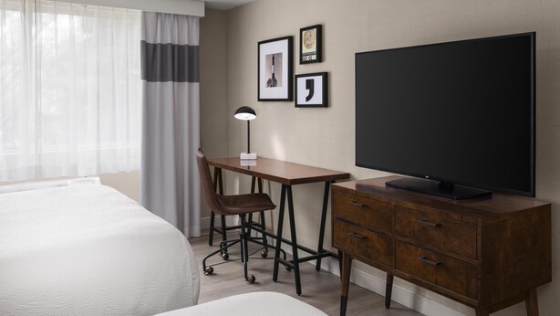 Quarto de hotel com cama, escrivaninha com cadeira, televisão e obras de arte na parede.