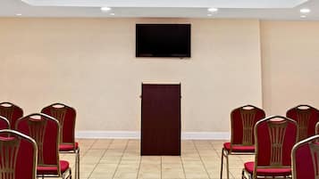 Sala de conferências com cadeiras vermelhas, um púlpito de madeira e uma TV de tela plana na parede.