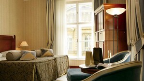 Quarto de hotel com cama, escrivaninha, cadeira, abajur e vista para um edifício pela janela.