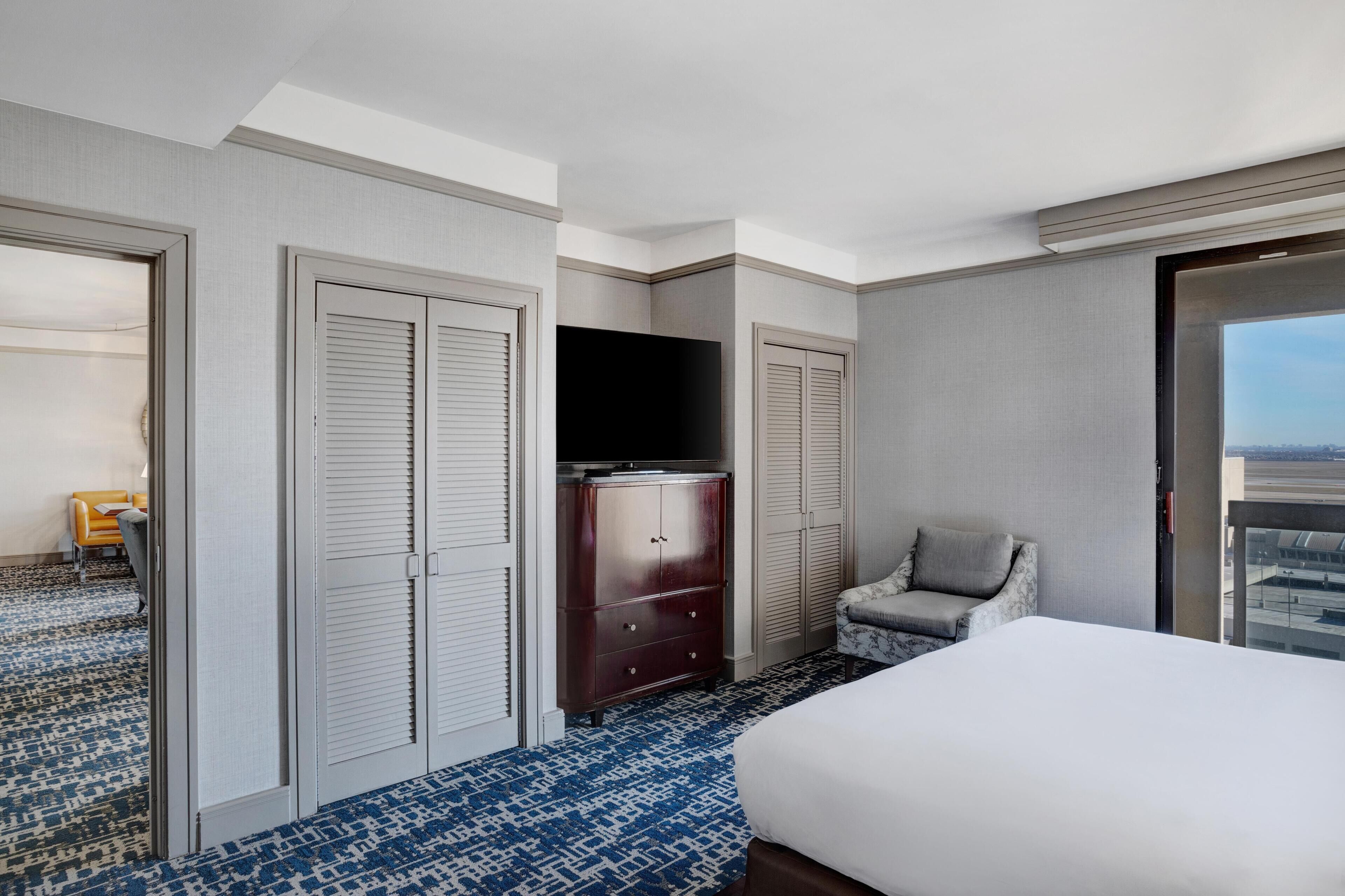 Quarto de hotel com cama, televisão, guarda-roupa, cadeira e vista da cidade.
