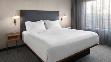 Quarto de hotel com uma cama grande, duas mesas de cabeceira e uma janela com cortinas.