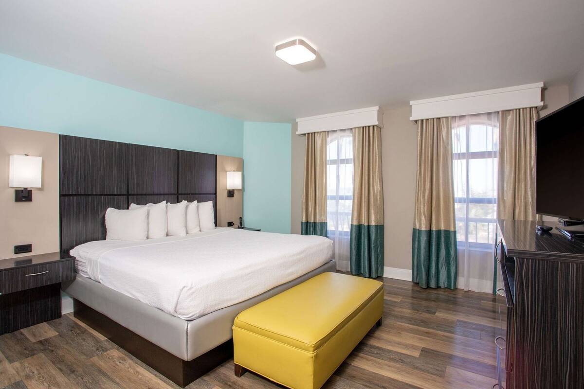 Quarto de hotel com uma cama grande, mesas de cabeceira, escrivaninha, cadeira e televisão.